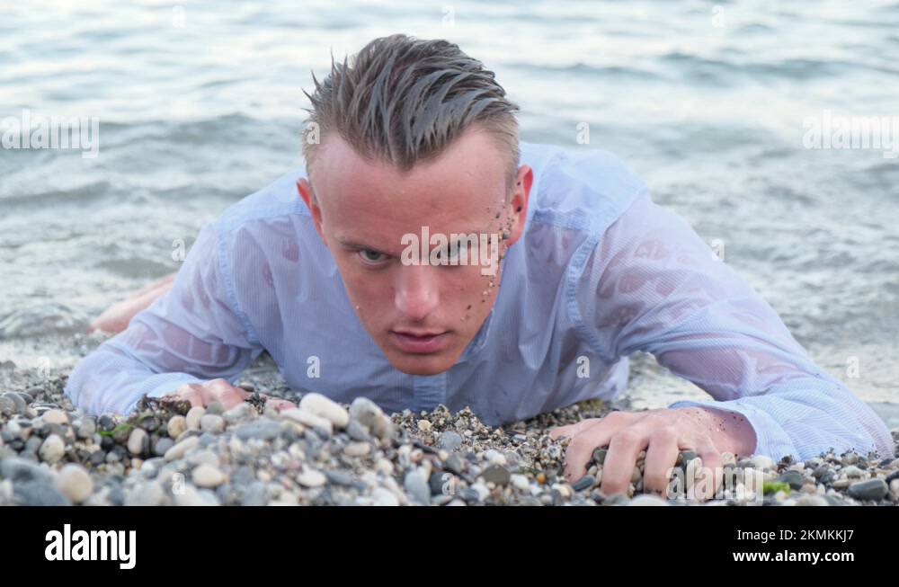 Exhausted Escaped Man After A Shipwreck Crawling Out Of The Sea To The