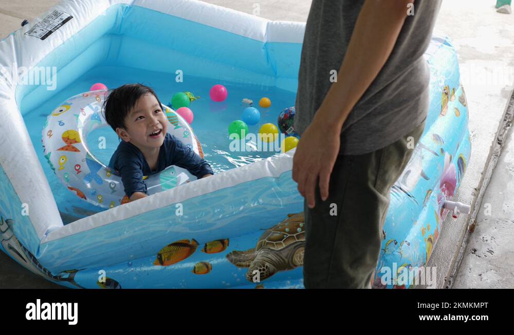 Asian cute child boy playing water splash to father in pool at home ...
