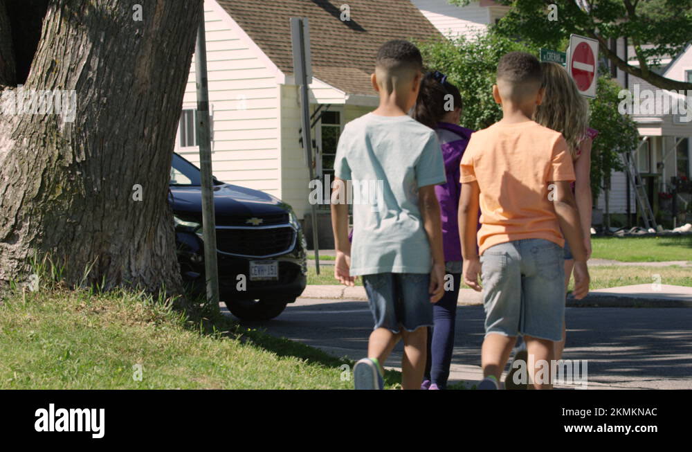 diverse group of kids meet a car at an intersection in neighbourhood ...