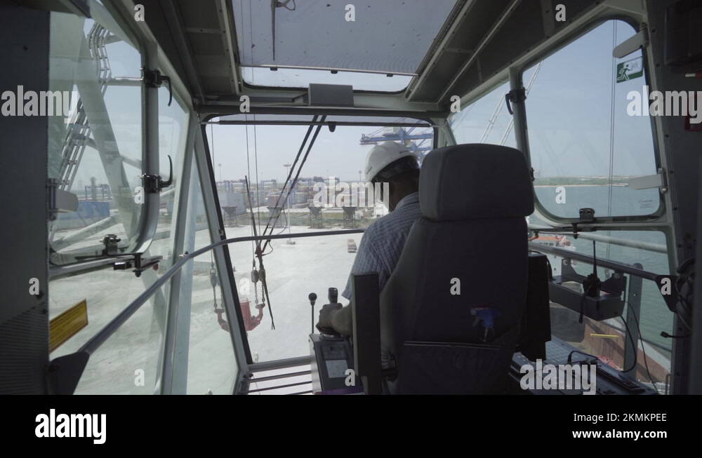 Operator in cab of tall tower crane signals to ground crew in sea port ...