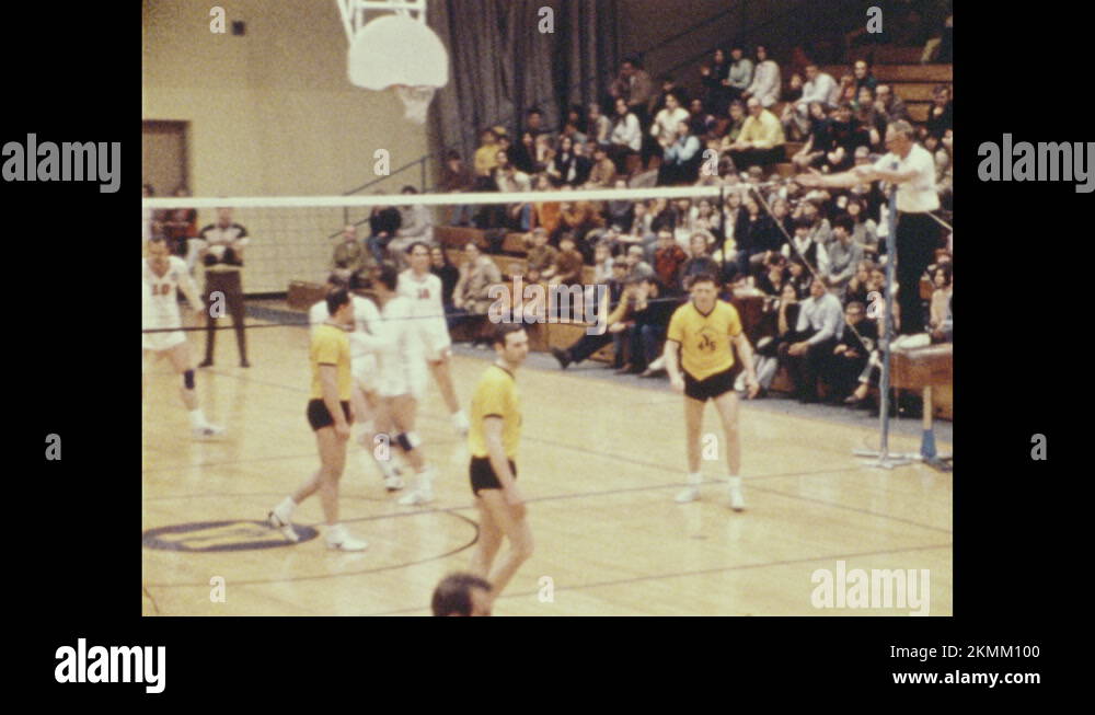 1970s: Two teams play volleyball on gymnasium court in front of crowd ...