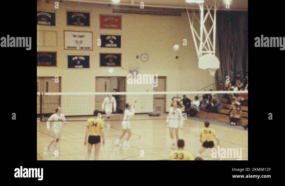 1970s: Two teams play volleyball on gymnasium court in front of crowd ...