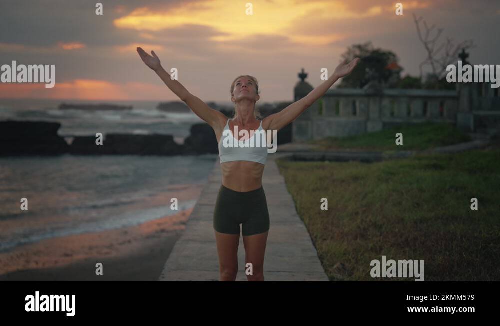 Woman lifting hands together in namaste yoga standing pose, sun ...