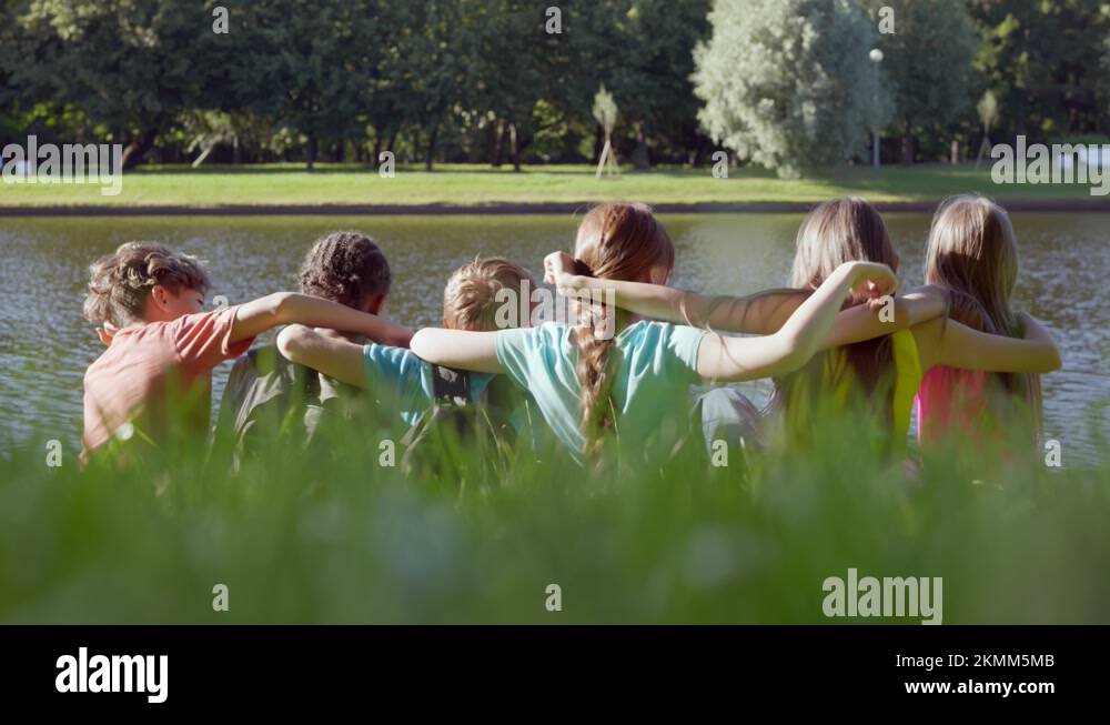 Back view of teenagers sitting on grass and hugging in summer park ...