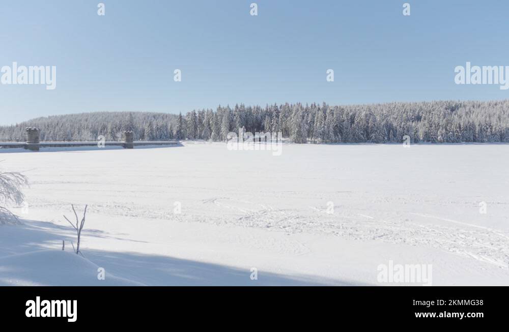 A frozen lake covered with snow with footprints - a dam and a forest in ...