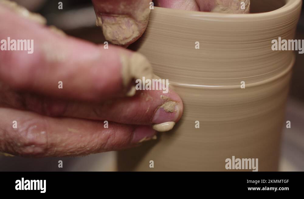 Artisans hands give the spinning clay on the potters wheel shape by ...