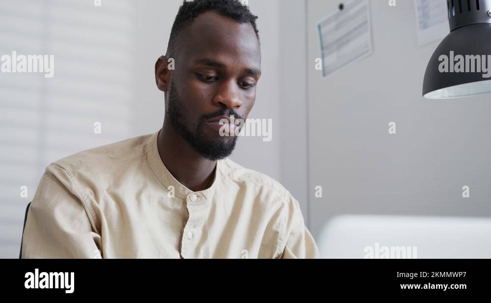 black man with a beard typing on a laptop, rubs his chin in reflection ...