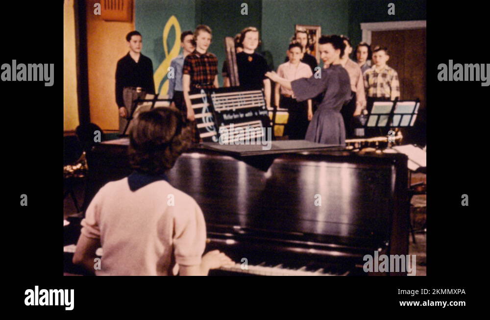 1950s: Classroom. Teacher conducts as students sing. Young woman plays ... 1950s: Classroom. Teacher conducts as students sing. Young woman plays ...
