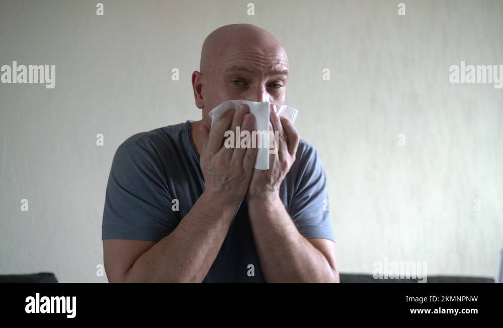 Unhealthy bald man. Guy is sick with flu, sneezes and blows his nose ...