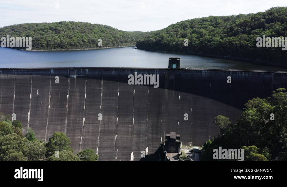 Drone ascends to reveal large dam full of water, surrounded by luscious ...