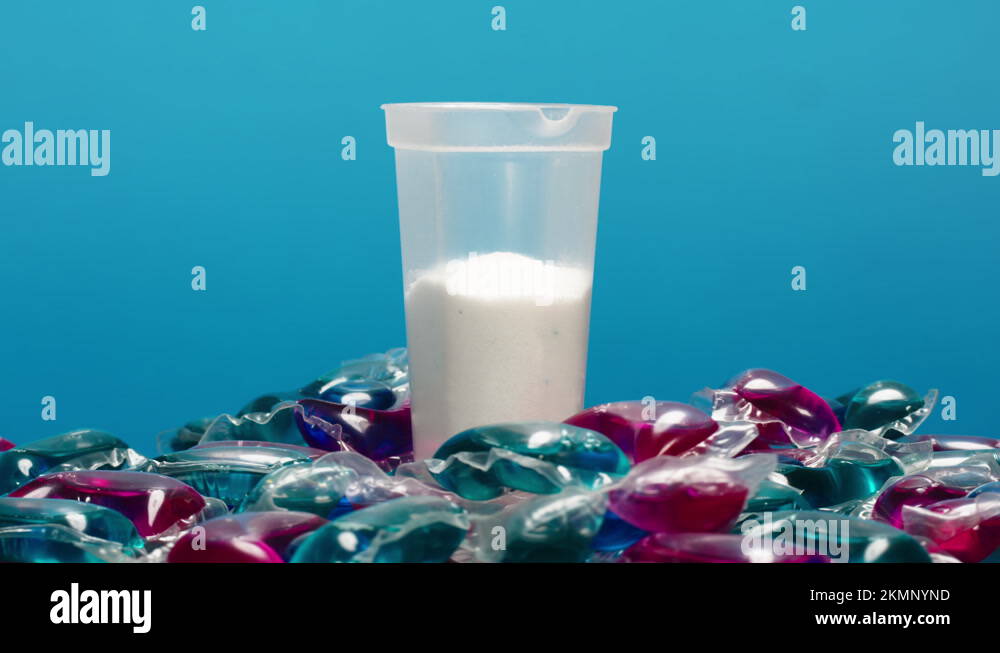Washing gel pods and plastic glass with detergent powder on blue ...