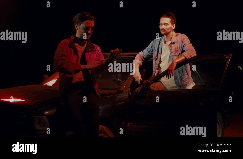 Two men in sunglasses dance vigorously outside car on the street at ...