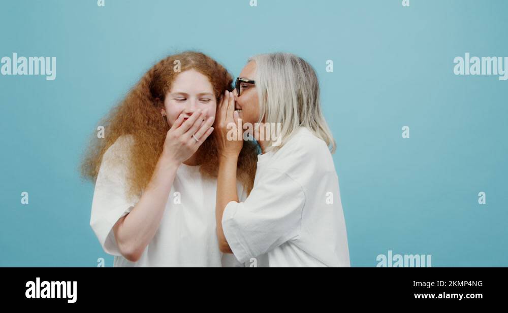 Aadult woman whispers in the ear of a young girl and they laugh ...