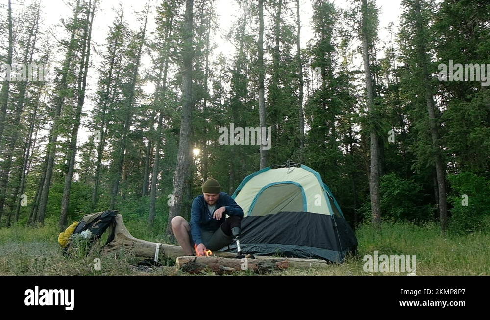 Disabled man with prosthetic limb is sitting on in forest near fire and ...