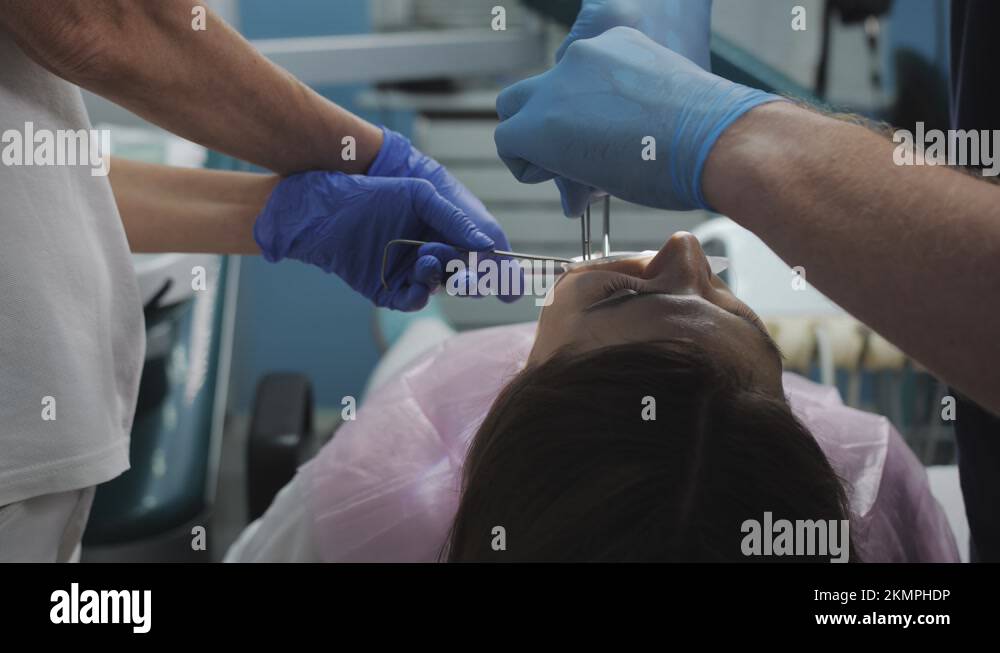 Face of patient, hands of dentist sutured wound after tooth extraction ...