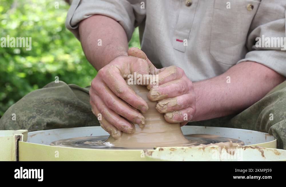 Caucasian male potter centers a piece of clay on a rotating circle and ...