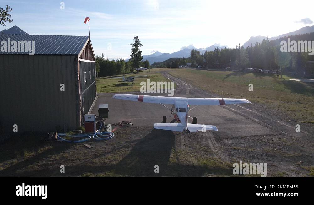 Slowly flying over a Cessna 206 next to a hanger over a private grass ...