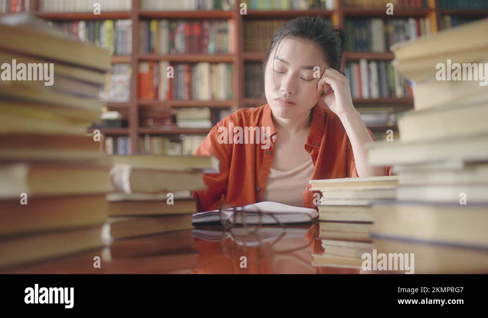 Upset asian female student sitting behind stacks of books, academic ...