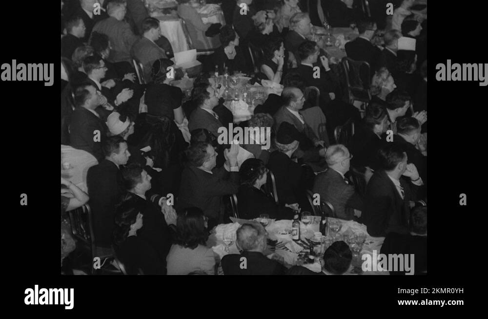 1940s:A crowd of people sitting around tables clap. People stand to ...