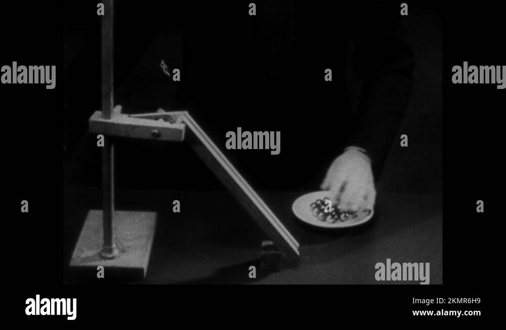 1950s: Man pours box of marbles on plate. Man rolls metal balls down ...
