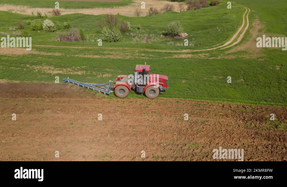 Red tractor with harrows is loosening the ground to protect soil from ...