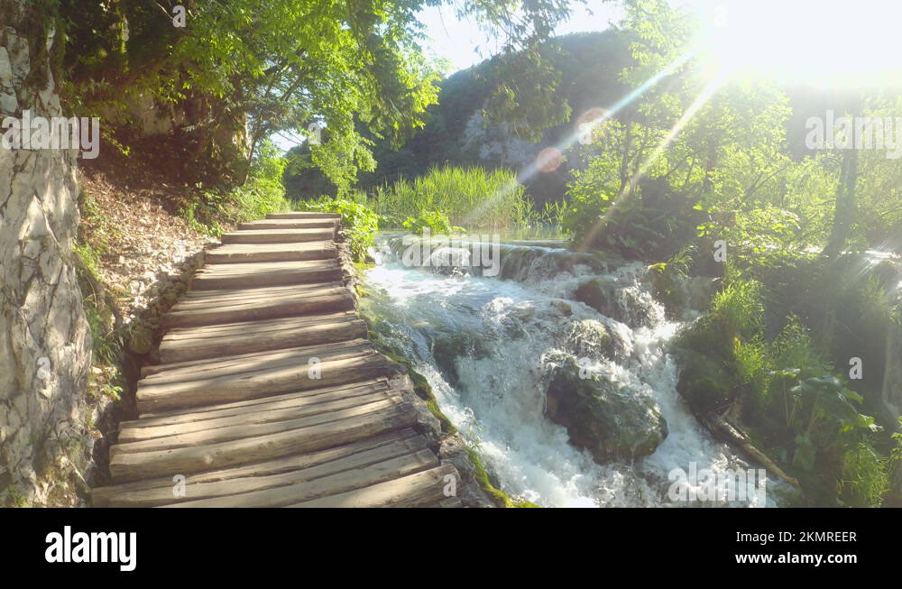LENS FLARE: Wooden steps lead up to the top of a sunlit waterfall in ...