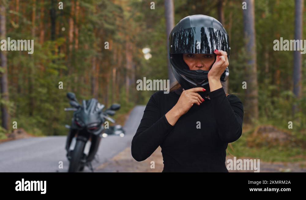Adult woman motorbike rider fixes her helmet and looking in the camera ...