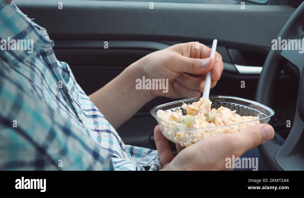 Man, sitting in a car, eats a salad with mayonnaise from plastic ...