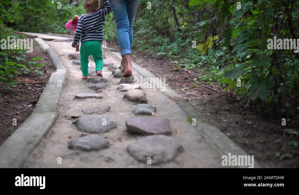 Barefoot children with mother walk on stones path. Path way in sensory ...
