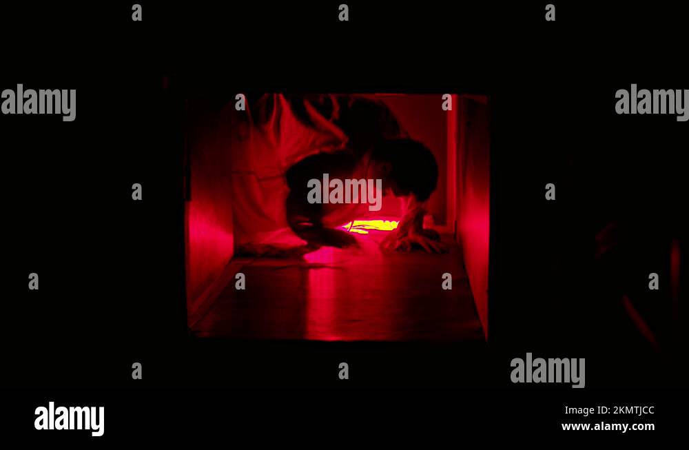 Scary man in straitjacket crawling in ventilation shaft in red lighting ...