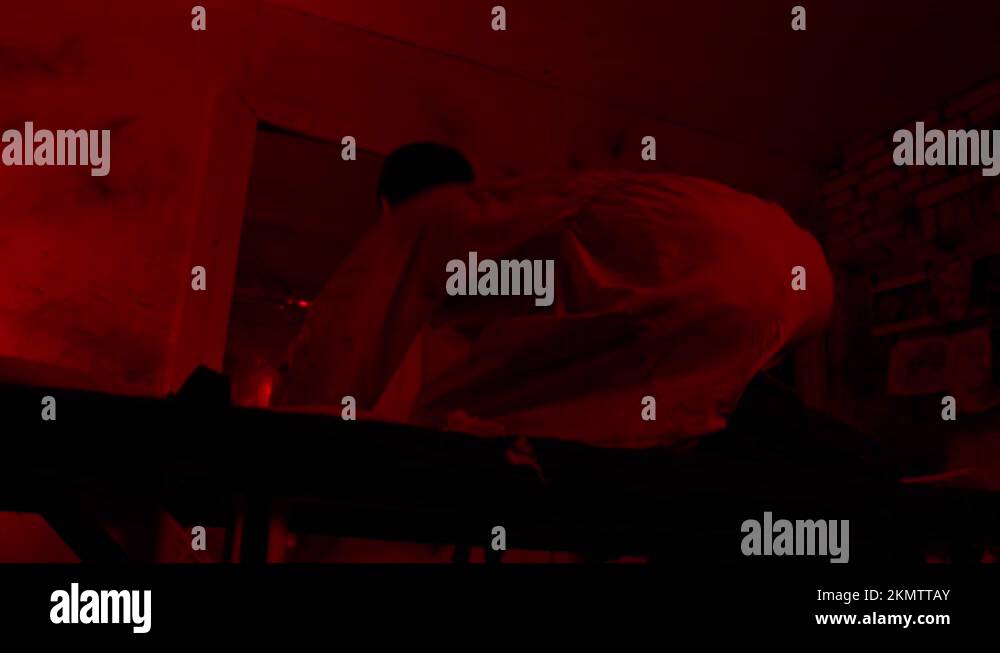 Mad man in straitjacket getting crazy sitting on the bed in the cell of ...