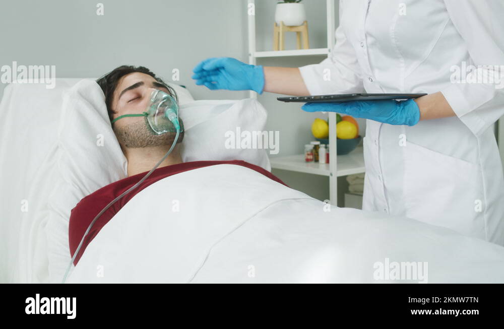 Doctor checking pulse of sick patient lying with oxygen mask in ...