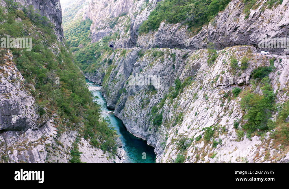 Canyon and road cut in its rocky wall, with a stream at bottom of deep ...