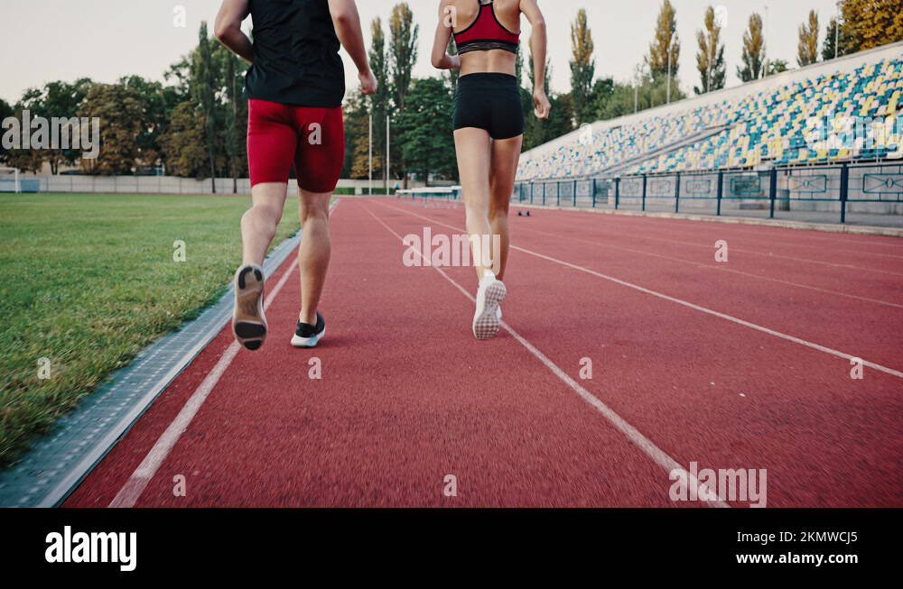 Back view fitness couple running on urban stadium together. Young man ...