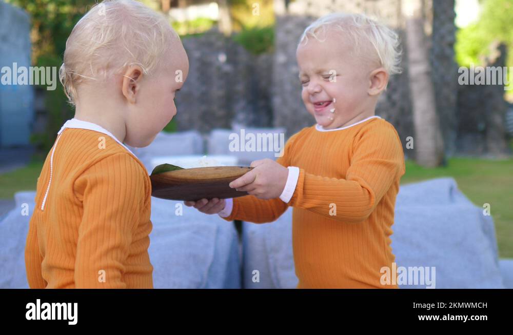 White twin girls eating rice from the wooden plate with no hands and ...