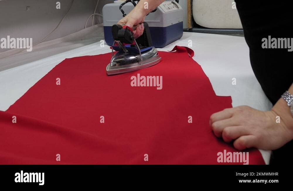 A dressmaker steams a new tailored dress on a specialized ironing board ...