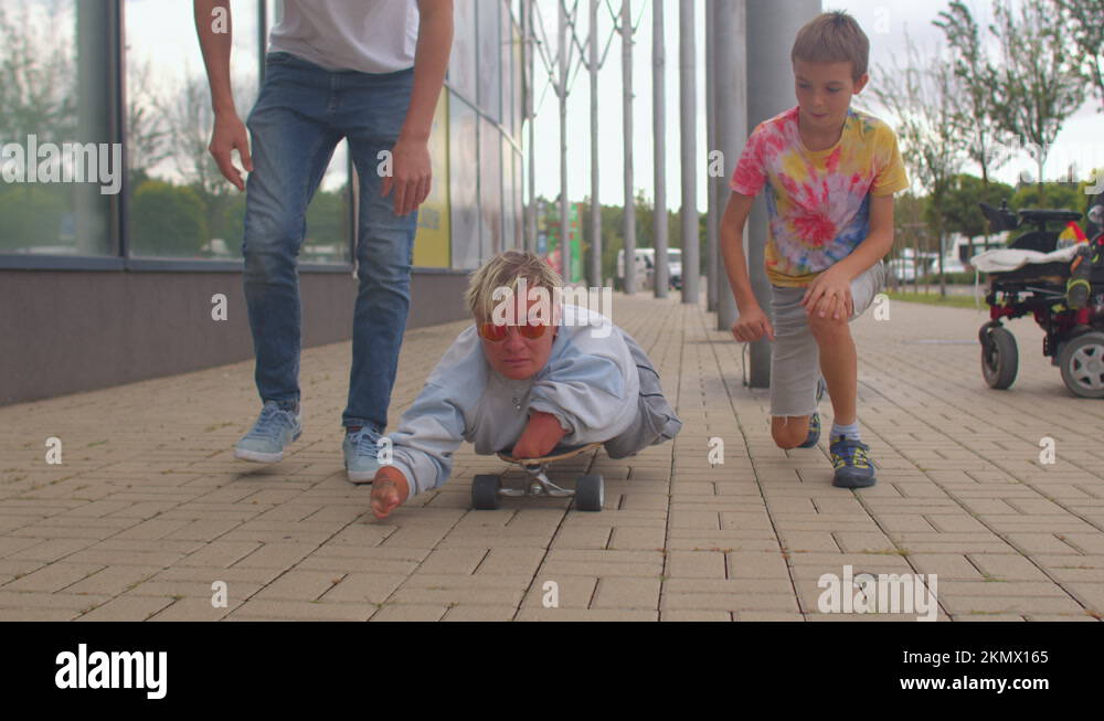 Two sons disabled person. She rolls on board sidewalk, guys walking ...