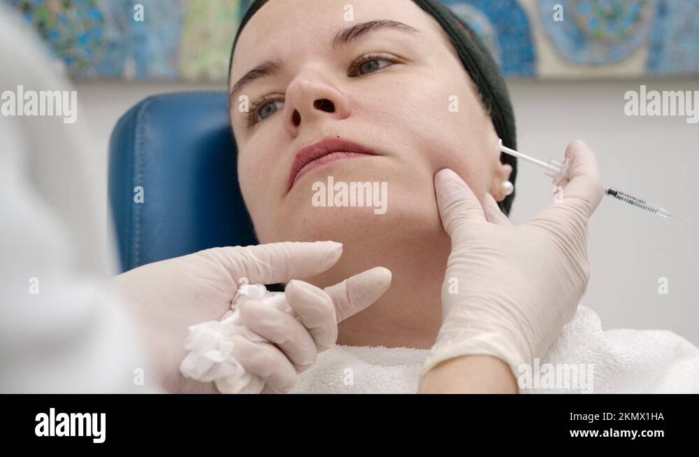Young woman receiving injection of botox, filler in lips, face closeup ...