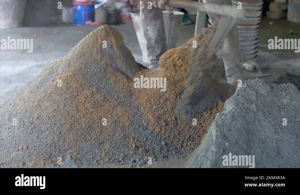 Hands of an Indian worker mixing cement and sand with the help of a hoe ...
