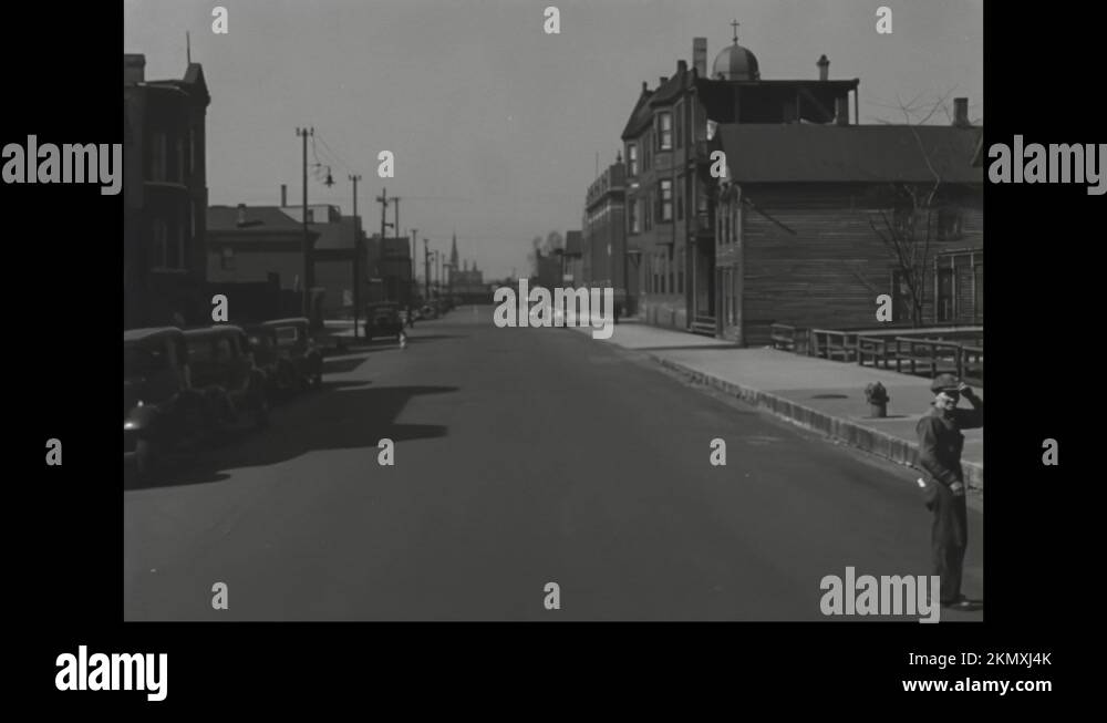 1940s: Street view of city neighborhood and road. Parked cars line the ...