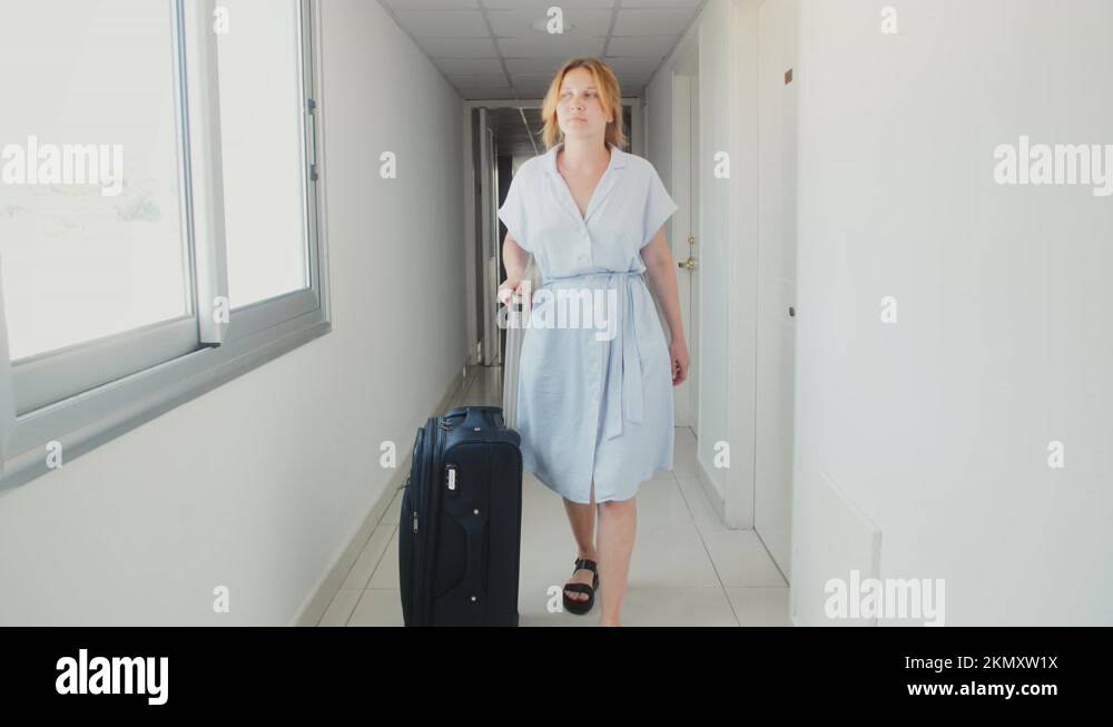 Guest walking at hotel corridor with baggage. Woman arriving in hotel ...