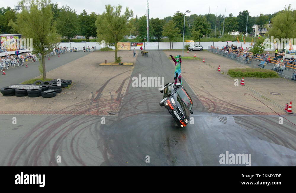Stuntman Standing On Top Side Of A Car Driving On Two Wheels In A Stunt ...