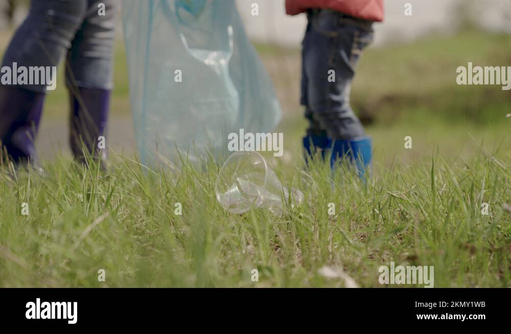 Little girl collects plastic garbage in the street in the green grass ...