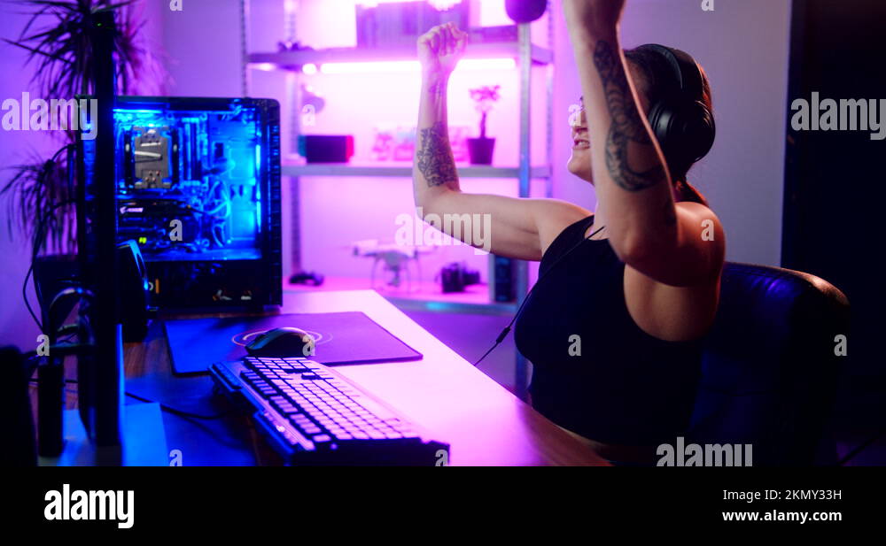 Girl gamer happily celebrates online computer at her gaming desk while ...