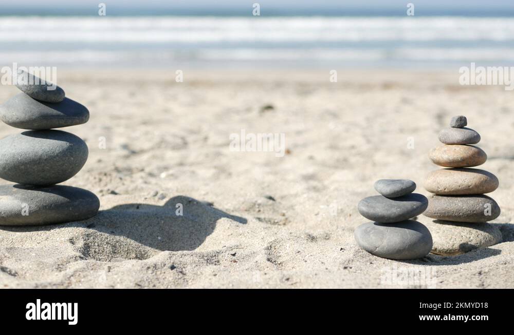 Rock balancing on ocean beach, stones stacking by sea water waves ...