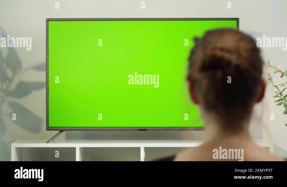 Woman watching TV with green screen in living room back view. Female ...