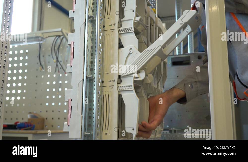 Factory worker is assembling a big electrical panel, plastic cover ...