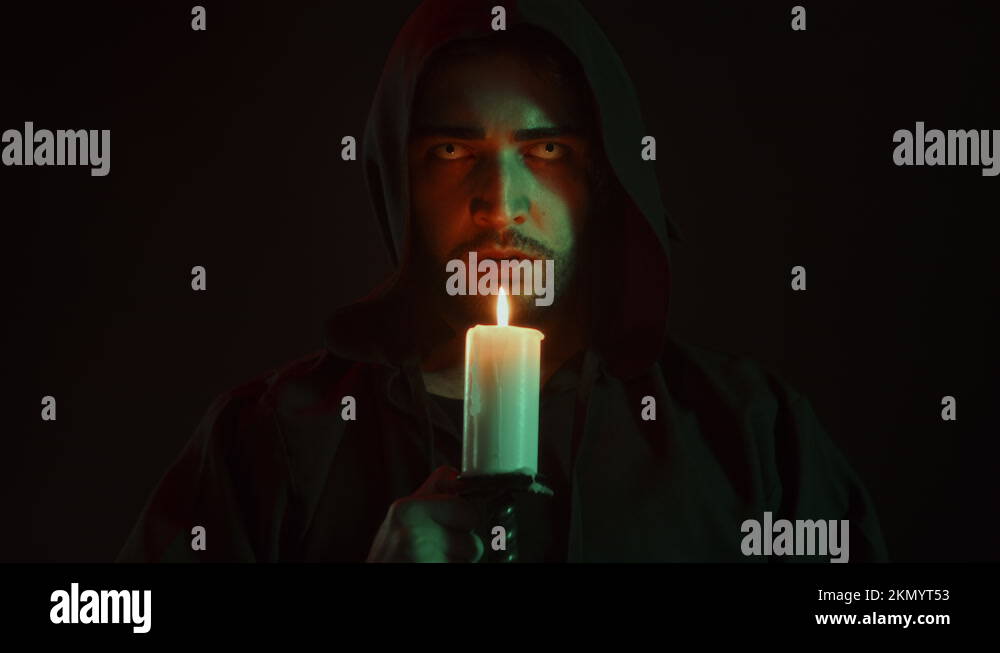 Evil sorcerer conjuring with burning candle, blowing flame out. Wicked ...