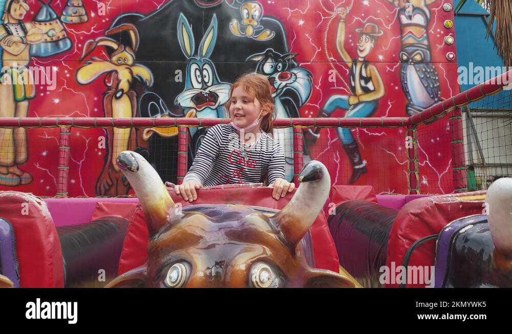 Redhead child girl having fun riding mechanical bull at amusement park ...