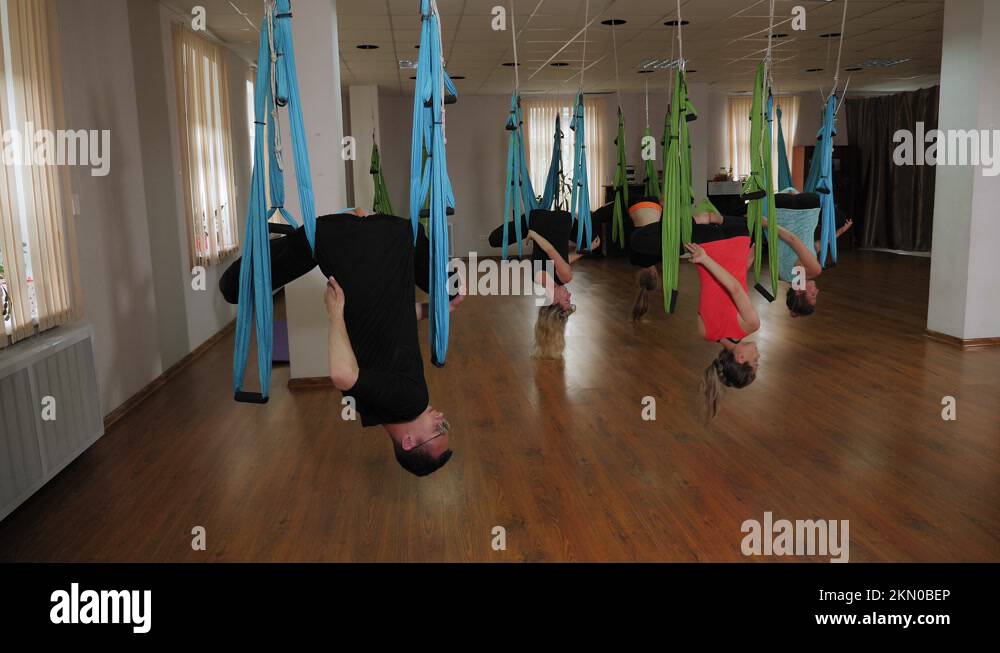 A group of people hang upside down in a hammock. Fly yoga class in the ...
